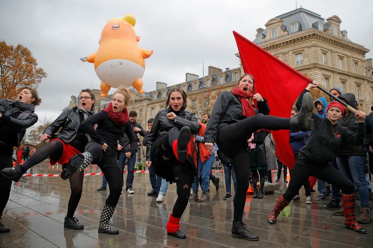People react in front of a large inflatable blimp depicting President Trump in Republique Square ...